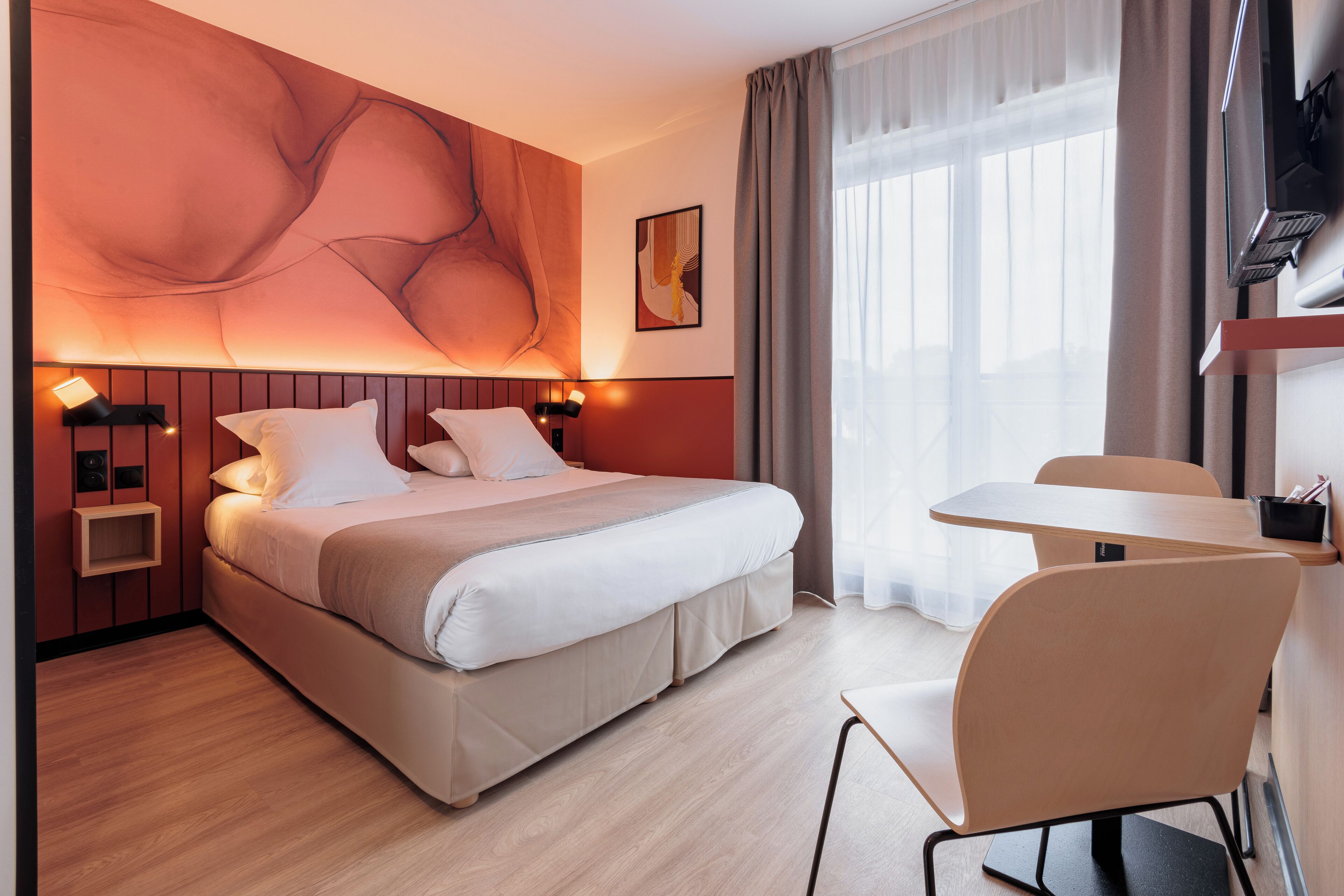 Quarto de hotel moderno com uma cama grande, mesas de cabeceira, escrivaninha e uma cadeira.