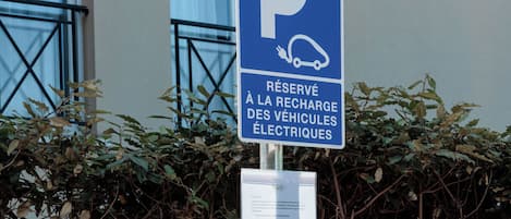 Sinal de estacionamento para carregamento de veículos elétricos, uma máquina de pagamento e um edifício com janelas e varanda.