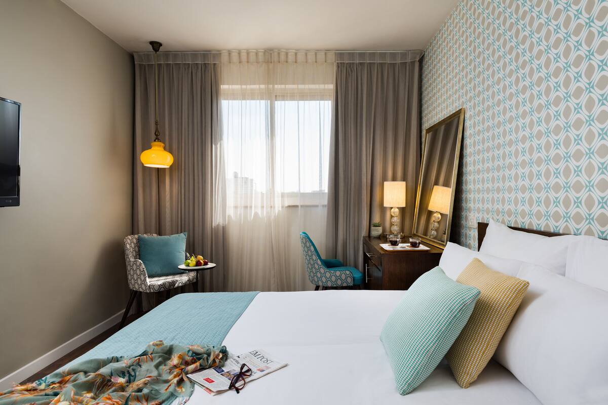 Quarto de hotel com cama, secretária com luminária, cadeira, televisão e janela com cortinas.