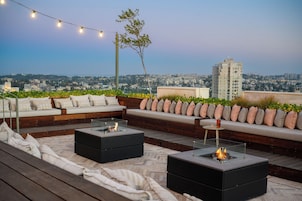 Uma área de estar externa com lareira, assentos acolchoados e vista para a cidade.