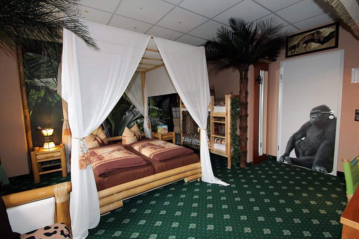 Quarto com cama sob dossel, uma mesinha com abajur, uma cadeira e um pôster grande na parede.