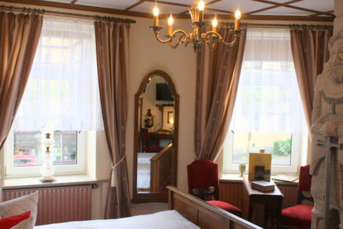 Quarto de hotel com uma cama grande, um lustre, um espelho e uma estátua.