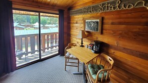 Interior de uma cabana de madeira com área de jantar, mesa, cadeiras, cafeteira e uma janela grande com vista para o exterior.