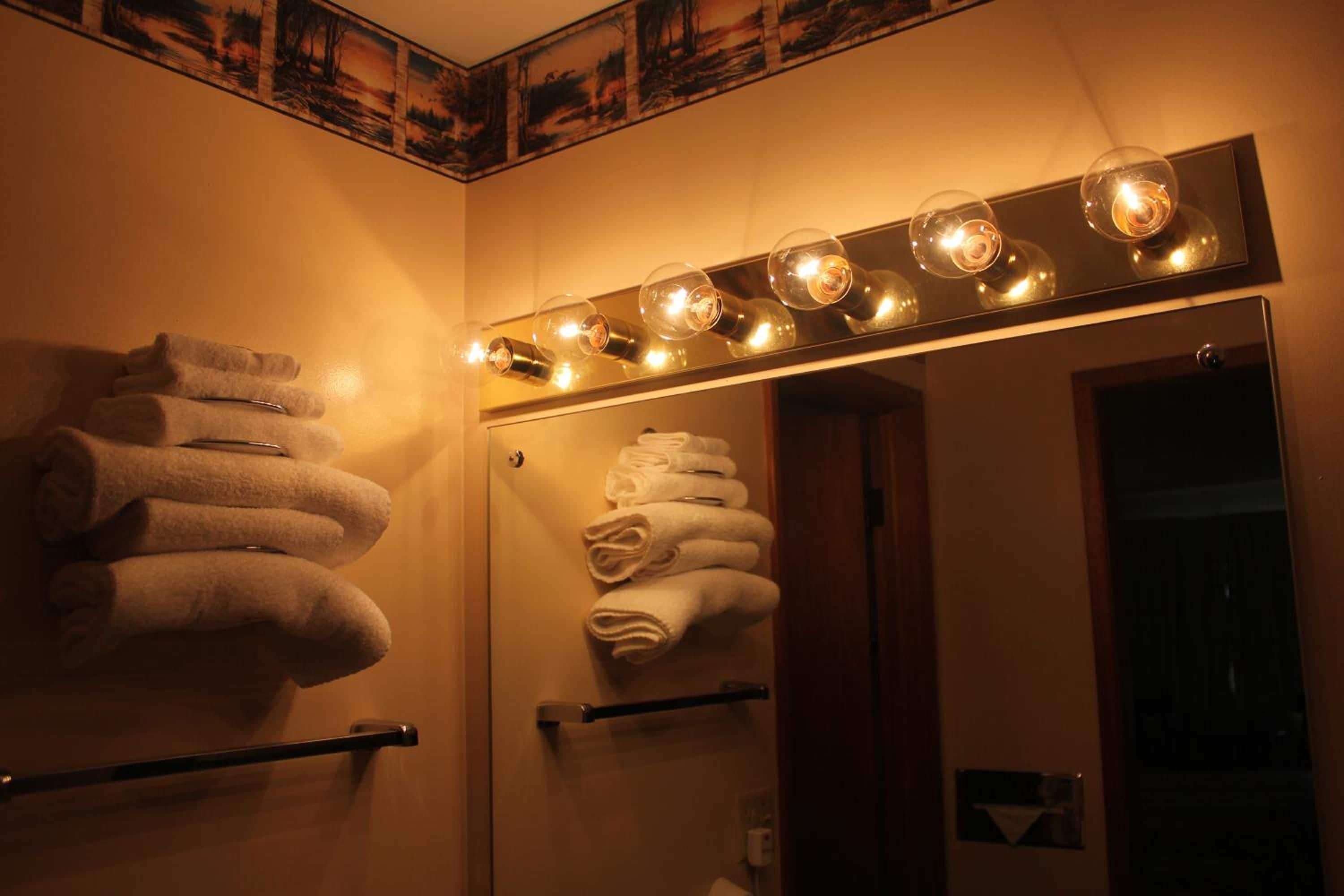 Casa de banho com espelho, porta-toalhas e luminária na parede.