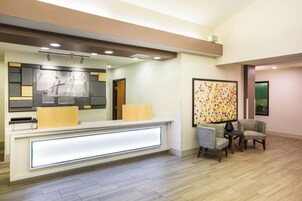 Uma área de recepção de hotel com um balcão moderno, um espelho grande e uma área de estar com duas cadeiras.
