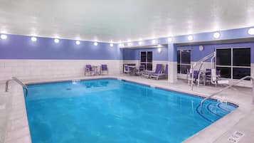 Piscina interna com água azul cristalina, rodeada por cadeiras de descanso roxas e um revestimento de azulejos.