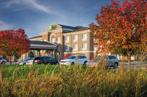 Um edifício Holiday Inn Express com fachada de tijolos, várias janelas e um estacionamento com diversos carros.