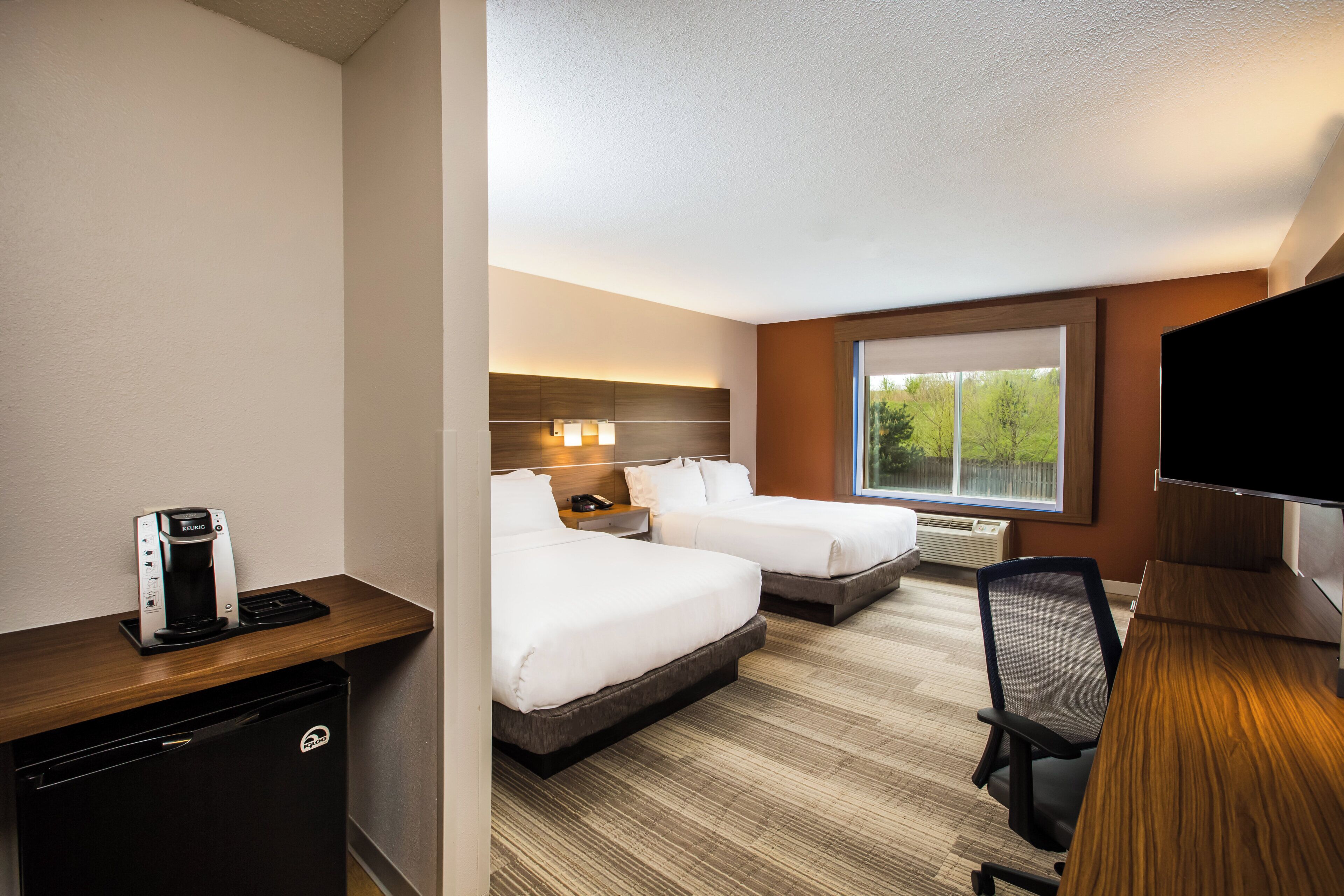 Quarto de hotel com duas camas, uma escrivaninha, uma televisão e uma cafeteira.