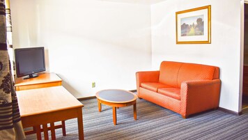Quarto com escrivaninha de madeira, televisão, mesa redonda, sofá laranja e um quadro na parede.