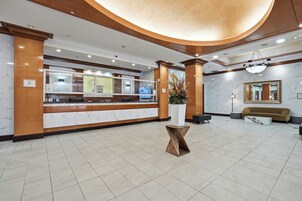 Um hall de hotel com uma mesa de recepção, um espelho grande e uma área de estar.