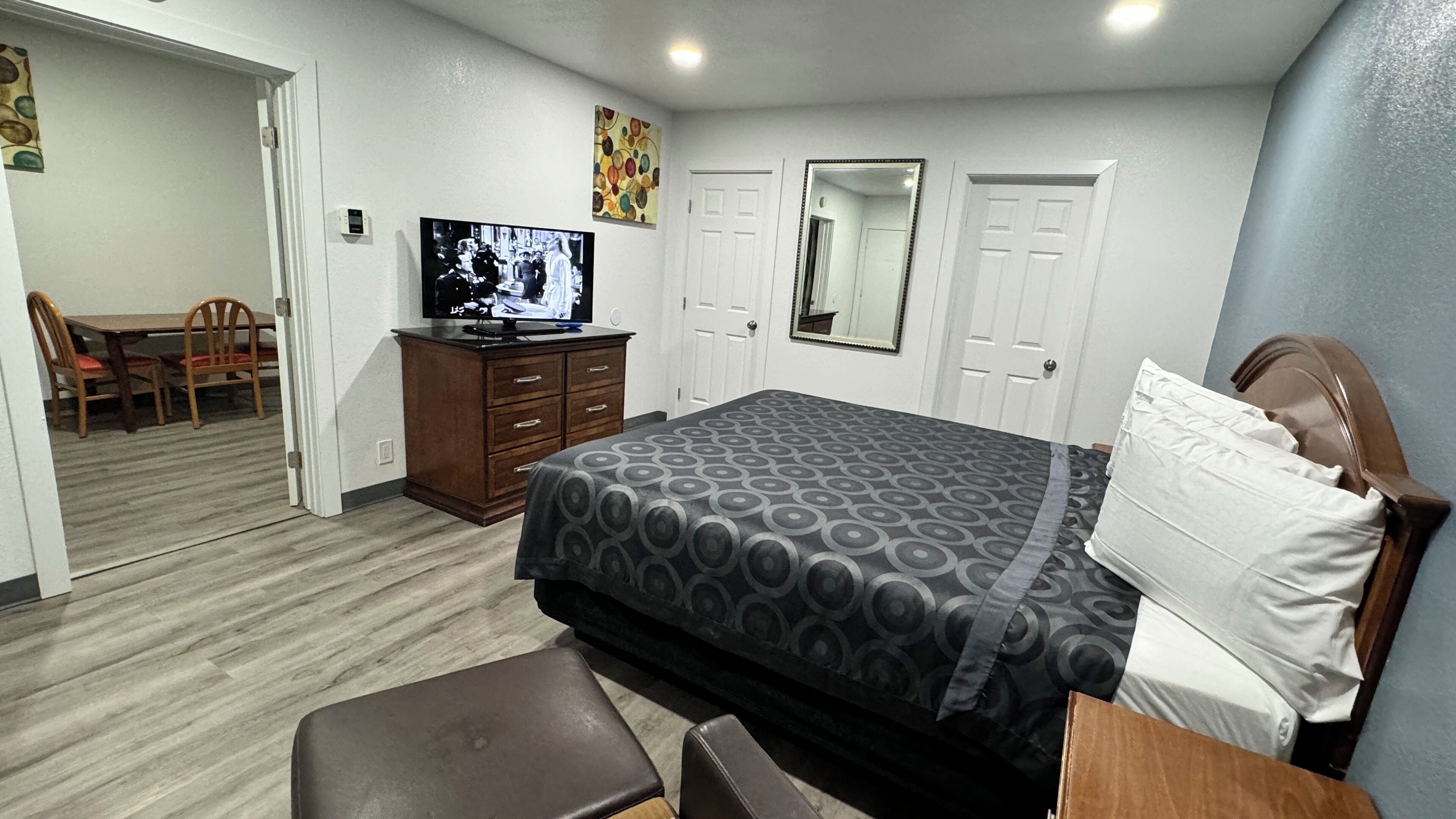 Quarto com cama, televisão, penteadeira, cadeira e porta.
