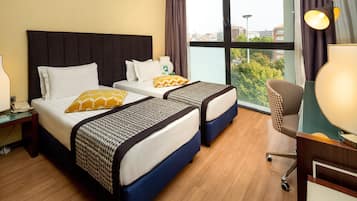 Quarto de hotel com duas camas, uma escrivaninha e uma janela grande com vista para a cidade.