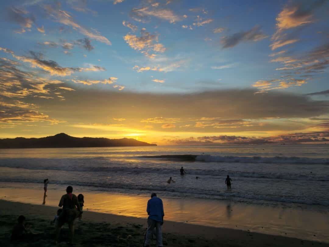 Uma praia ao pôr do sol, com pessoas.