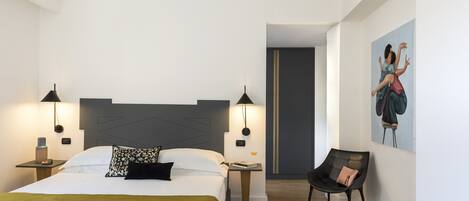 Quarto de hotel moderno com uma cama grande, duas mesas de cabeceira com luminárias, uma cadeira e um quadro na parede.