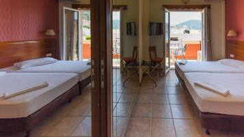 Quarto de hotel com duas camas, varanda com mesa e cadeiras, e vista para a paisagem urbana.