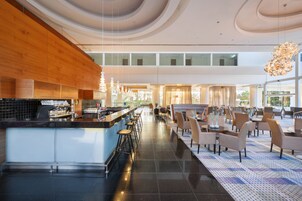 Um lobby de hotel moderno com área de bar, assentos e grandes janelas.