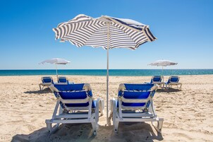 Uma praia com guarda-sóis listrados e cadeiras de praia azuis.