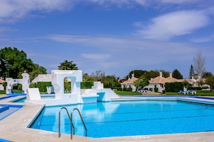 Piscina azul límpida com escadas de acesso, rodeada por estruturas brancas e vegetação.