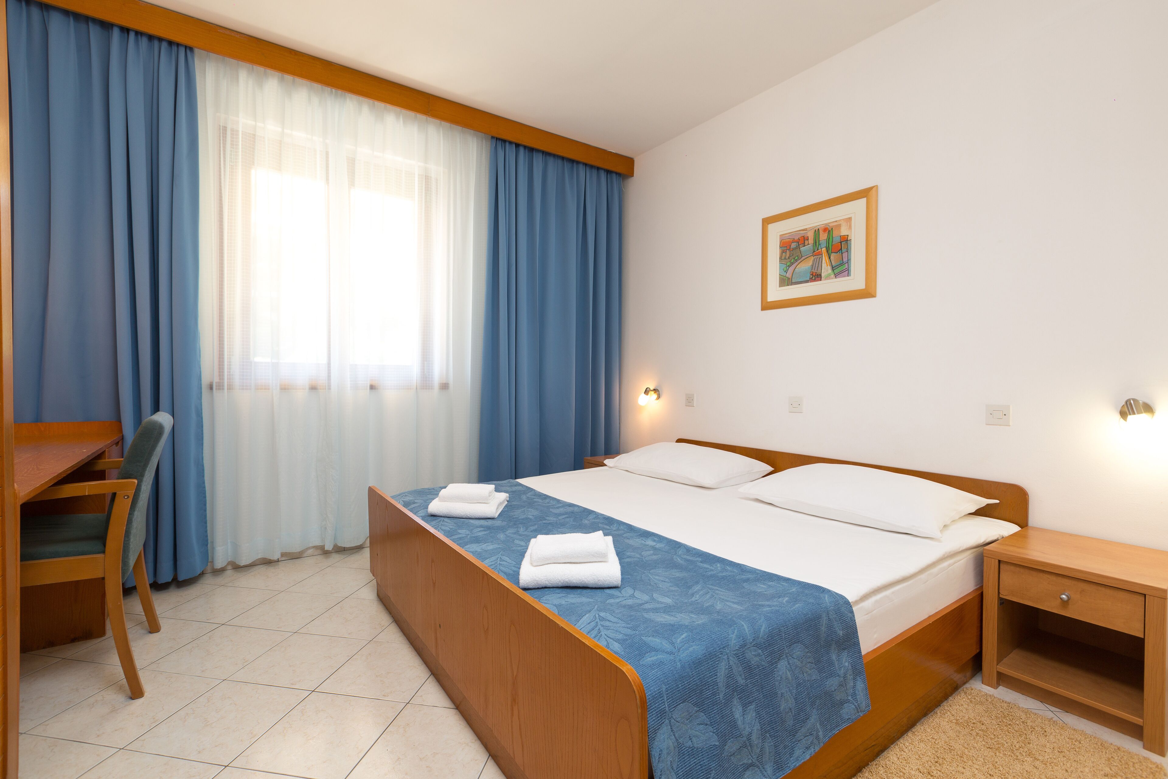Quarto de hotel com uma cama, uma escrivaninha e uma cadeira.
