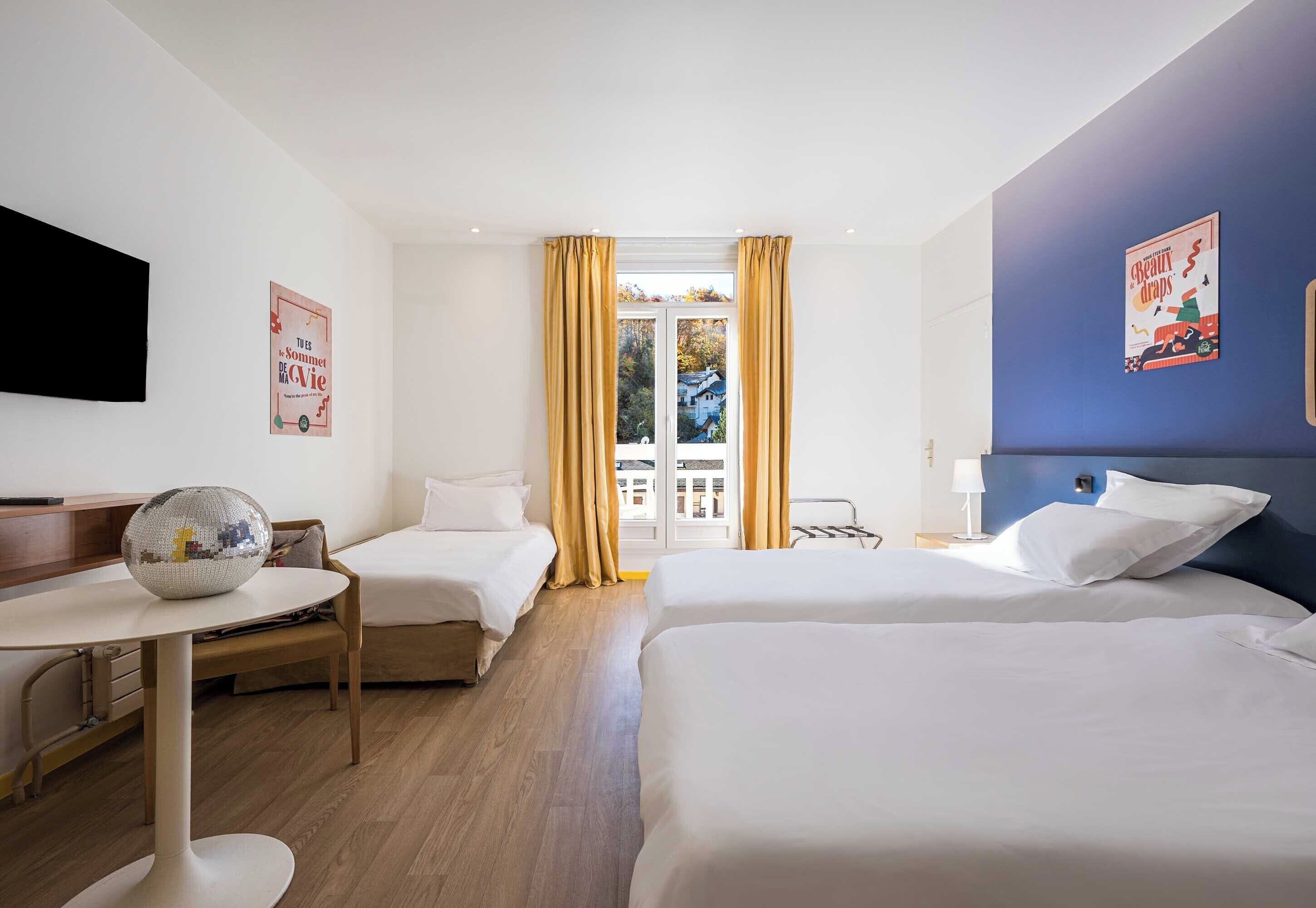 Quarto de hotel com duas camas, uma escrivaninha, uma cadeira, televisão e vista para o exterior.
