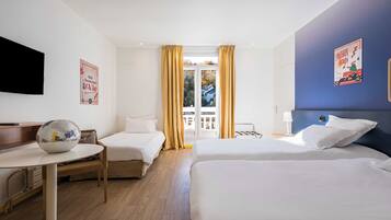 Quarto de hotel com duas camas, uma escrivaninha, uma cadeira, televisão e vista para o exterior.