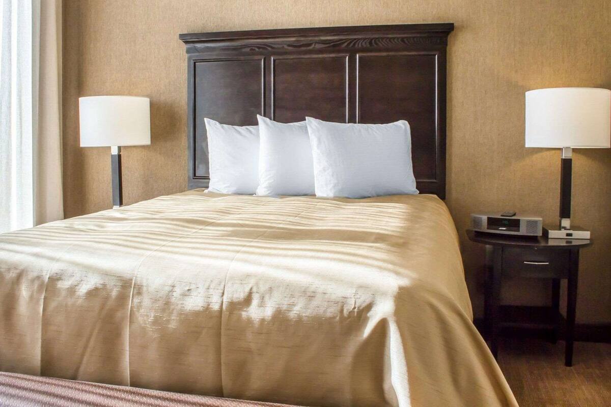 Quarto de hotel com uma cama grande, duas mesas de cabeceira com abajures e uma televisão fixada na parede.