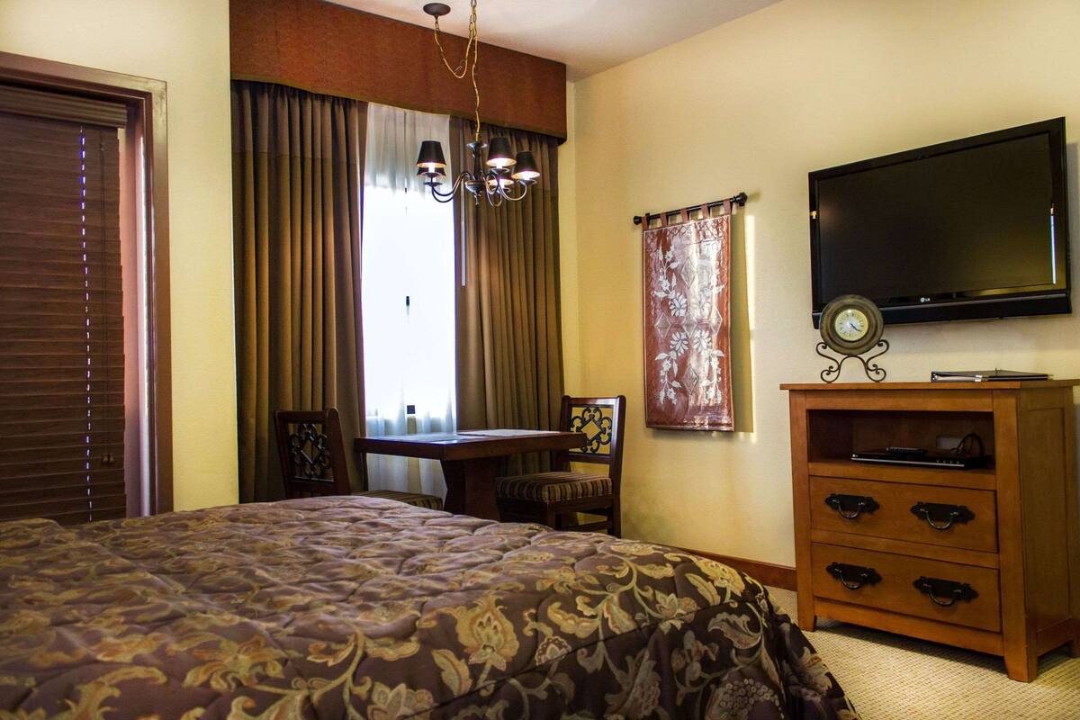 Quarto de hotel com uma cama grande, uma escrivaninha, uma cadeira, uma televisão e um armário.