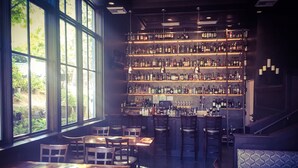 Um bar com várias prateleiras de garrafas, mesas e cadeiras dispostas para os clientes.