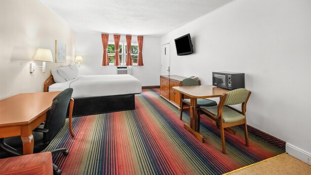 Quarto de hotel com cama, escrivaninha, cadeira, televisão e um tapete listrado e colorido.