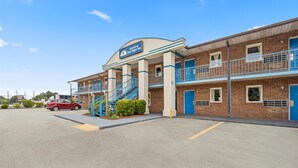 Um edifício de dois andares em tijolo com fachada azul e branca, um letreiro com a inscrição "Americas Best Value Inn" e um carro vermelho estacionado no estacionamento.