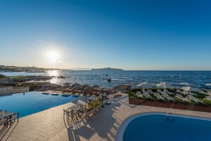 Área de piscina do resort com espreguiçadeiras e guarda-sóis, com vista para o mar.