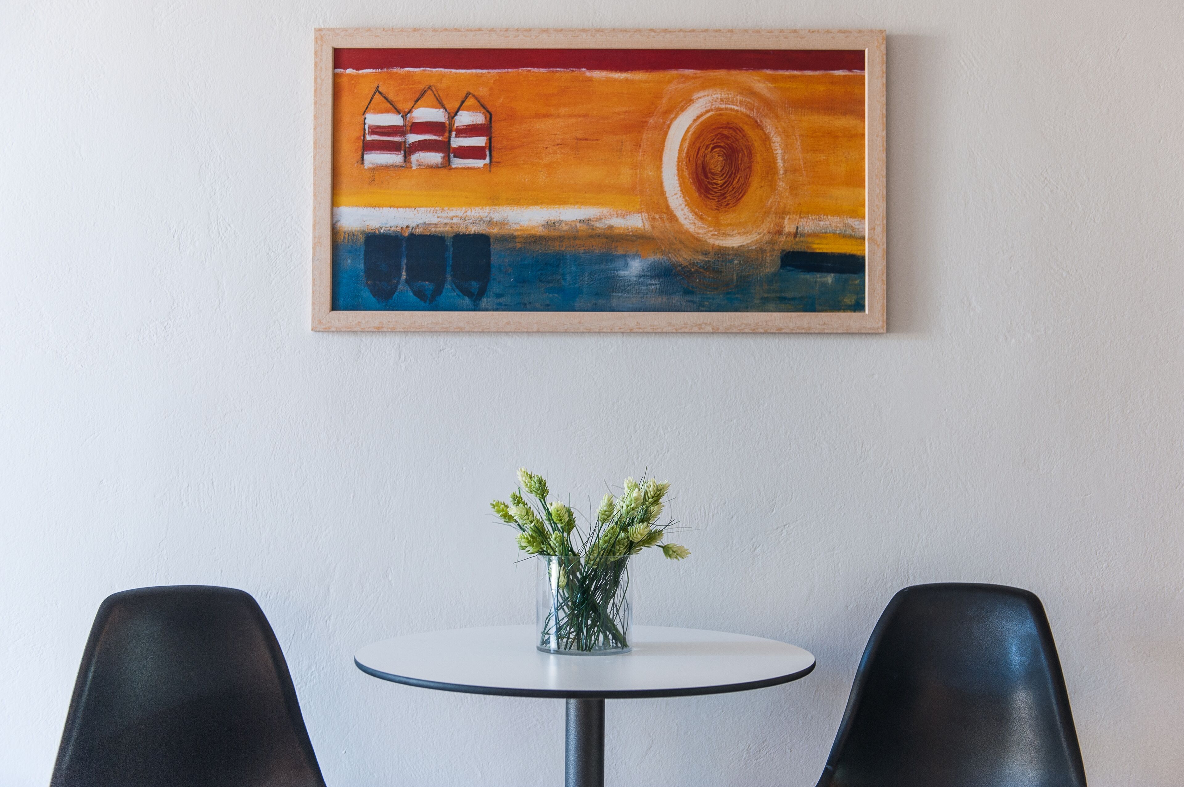 Um quarto com uma mesa redonda, duas cadeiras pretas e um quadro na parede.