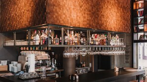 Uma área de bar com prateleiras de garrafas e copos, uma máquina de café e uma parede de tijolos.