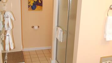 Um banheiro com chuveiro de vidro, porta-toalhas com toalhas, um quadro na parede e uma lixeira.