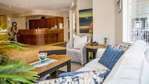 Um hall de hotel moderno com uma mesa de recepção, uma cadeira de vime, um sofá e uma janela ampla.