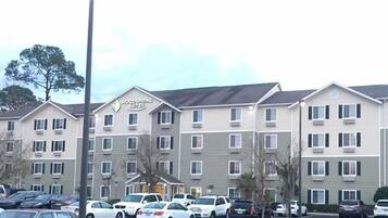 Um hotel com vários andares e uma placa indicando 'Woodspring Suites'. Vários carros estão estacionados no estacionamento, e o edifício apresenta um estilo arquitetônico moderno, com telhado plano e várias janelas.