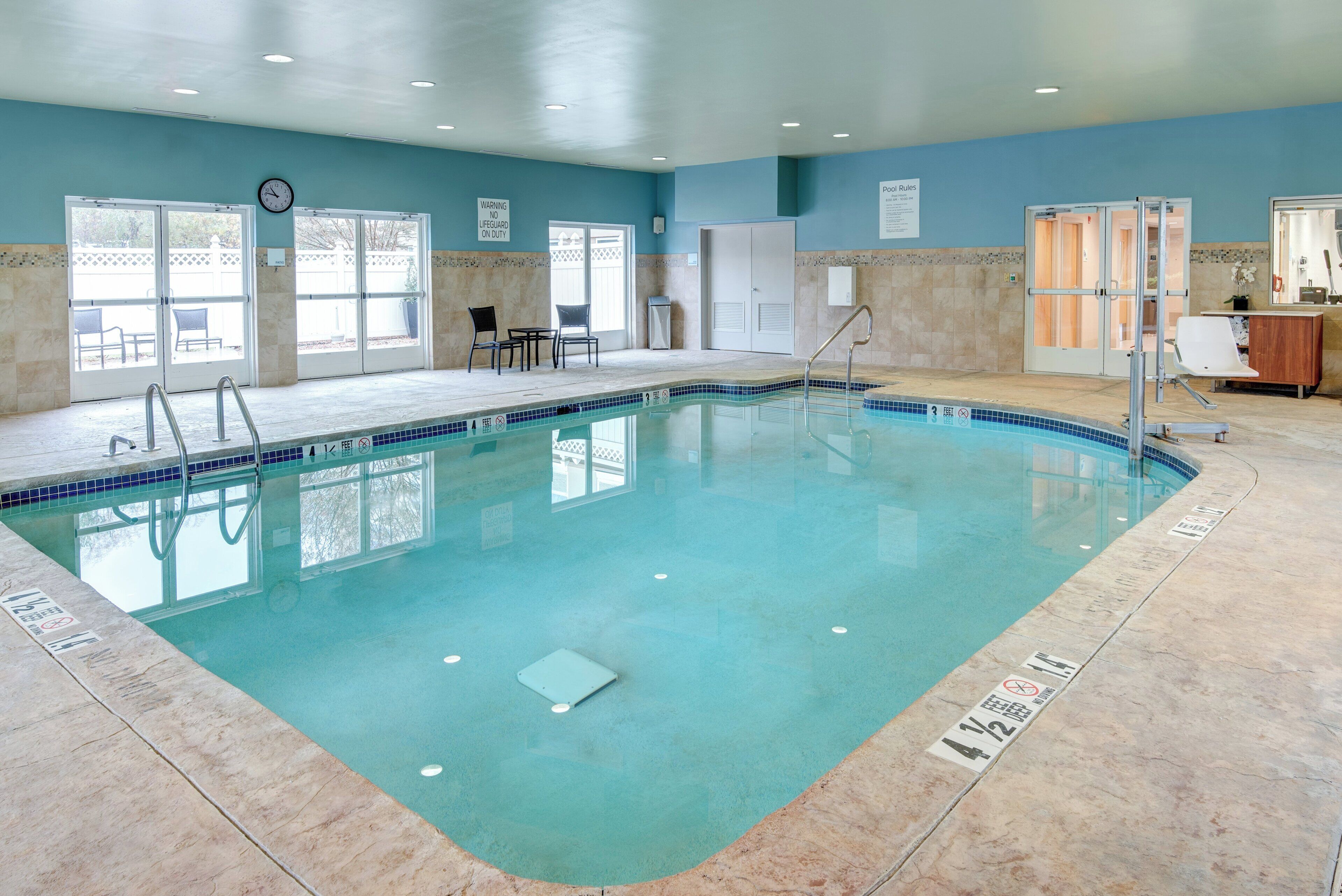 Piscina interior com água cristalina, marcações de profundidade e aviso de salva-vidas em serviço.