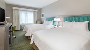 Quarto de hotel com duas camas, uma mesa com televisão, uma cadeira e janela com cortinas.