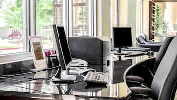Uma mesa de escritório moderna com um computador, monitor, teclado e rato. Um aviso indica que materiais adicionais estão disponíveis na recepção.