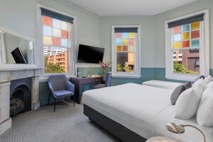 Quarto de hotel com cama, escrivaninha, cadeira, televisão e lareira.