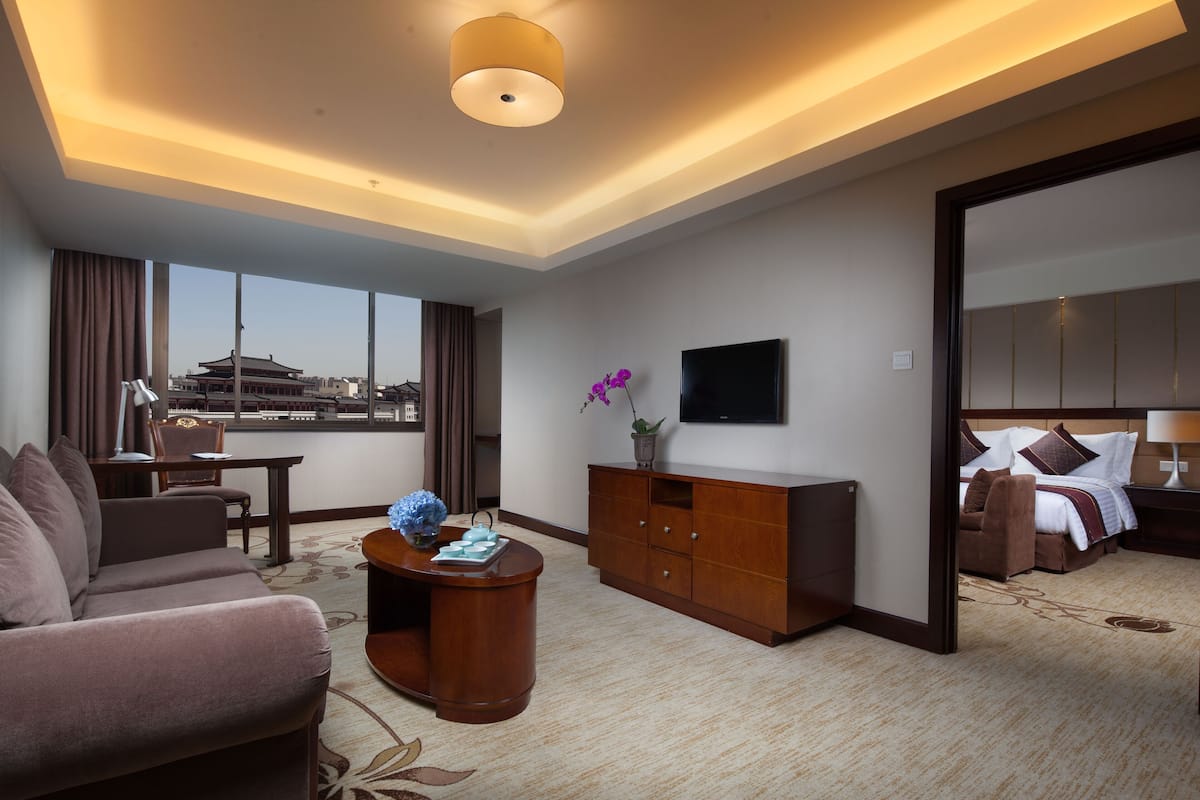 Quarto de hotel com sofá, escrivaninha, televisão, guarda-roupa e cama.