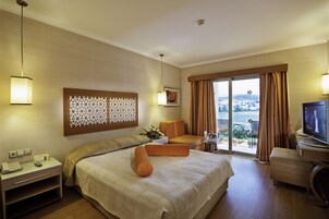 Quarto de hotel com uma cama grande, uma escrivaninha com luminária, televisão e varanda com vista.