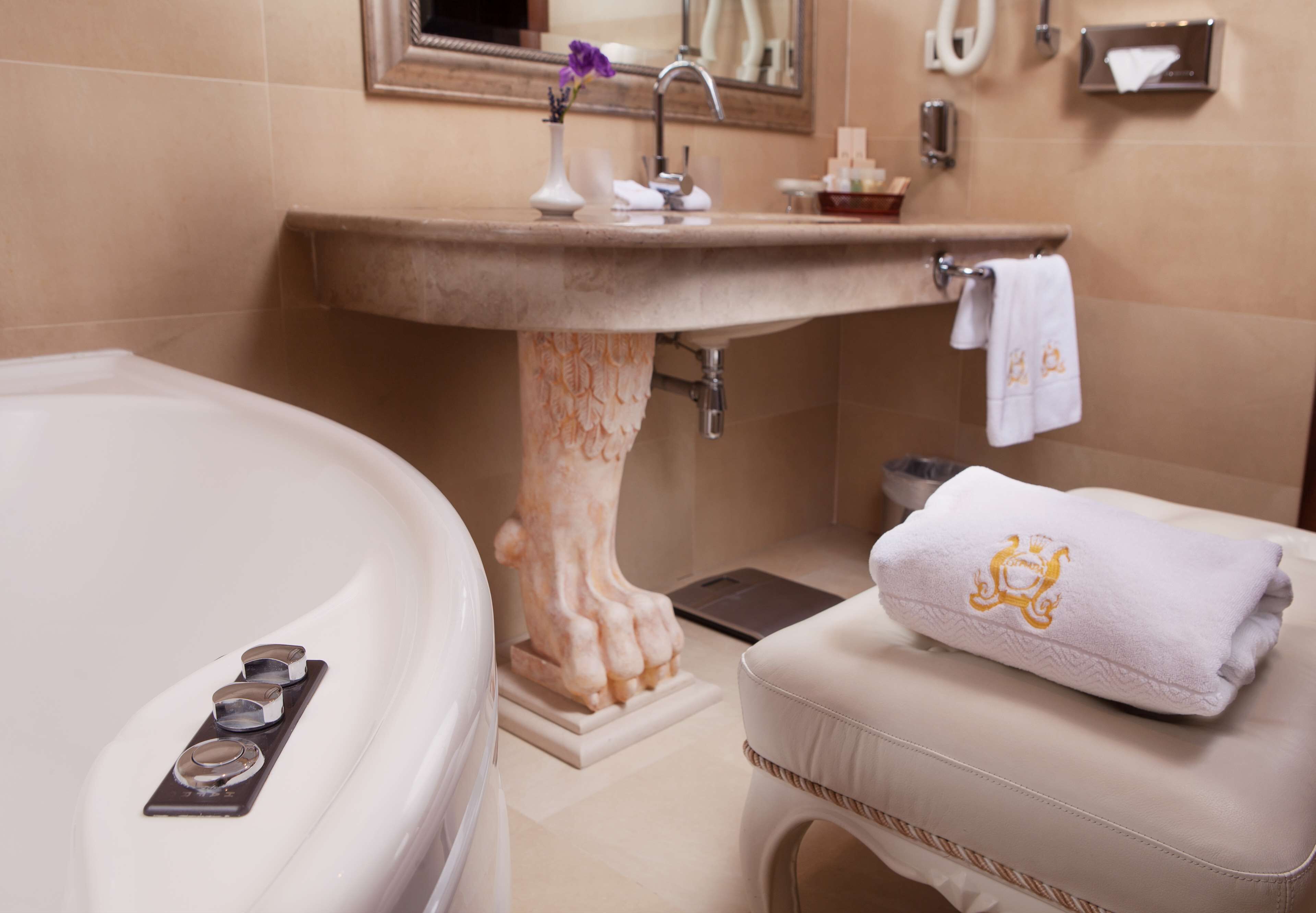 Uma casa de banho com uma pia de mármore, uma banheira e uma toalha sobre um banco.