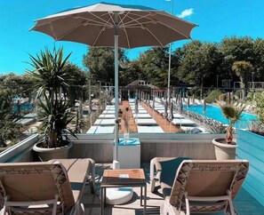 Uma área à beira da piscina com espreguiçadeiras, uma mesa e um guarda-sol.