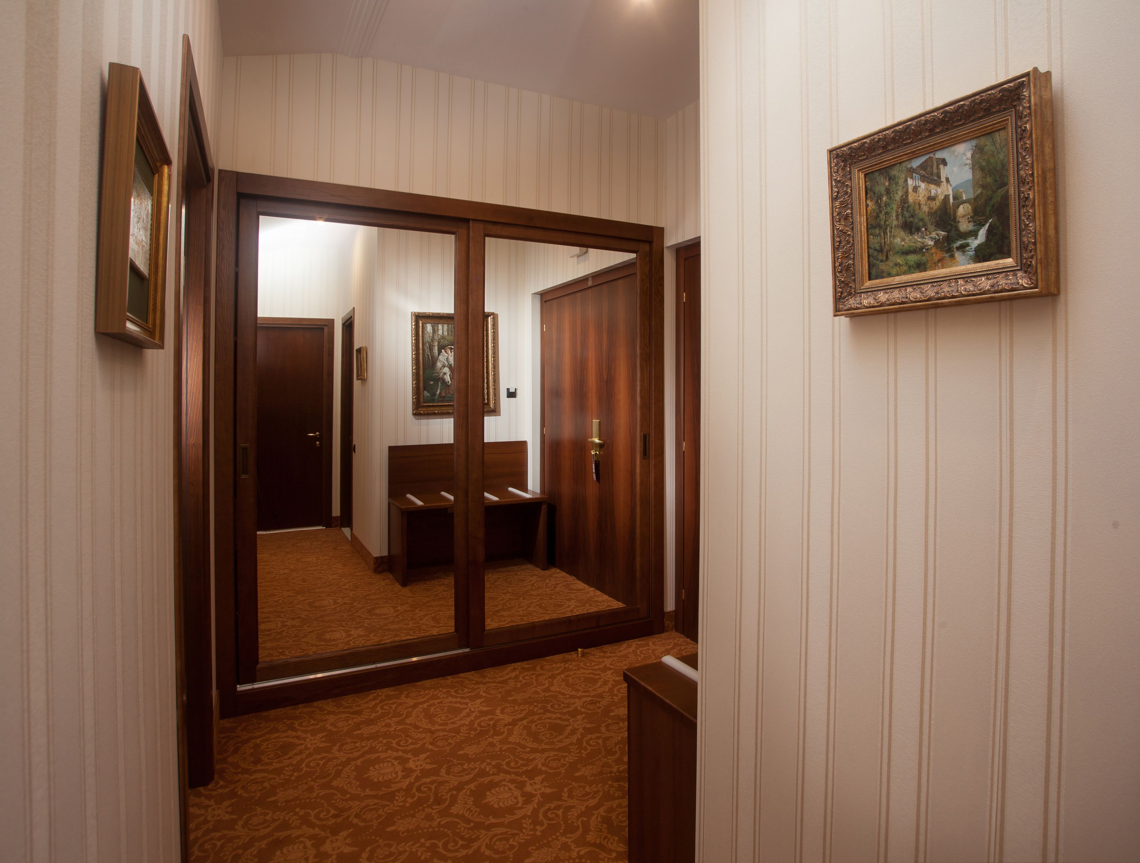 Um corredor com porta de madeira, um banco e um quadro na parede.