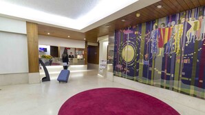 Um hall moderno com balcão de recepção, um tapete vermelho grande e um mural colorido na parede.
