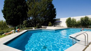 Piscina retangular com água azul cristalina, rodeada por um deck revestido com azulejos.