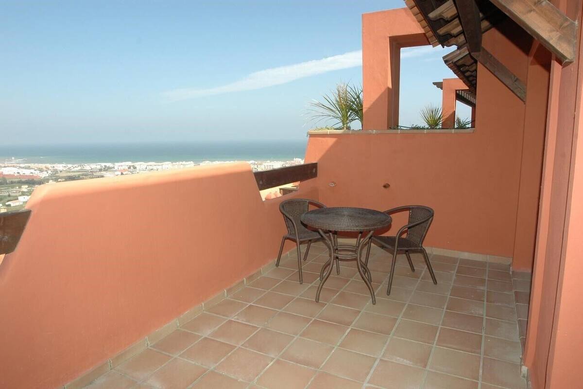 Varanda com vista para o mar, uma mesa redonda com cadeiras e chão de azulejos.