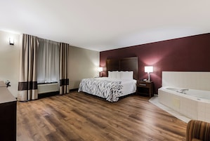 Quarto de hotel com cama, luminárias de cabeceira, banheiro com banheira e piso de madeira.