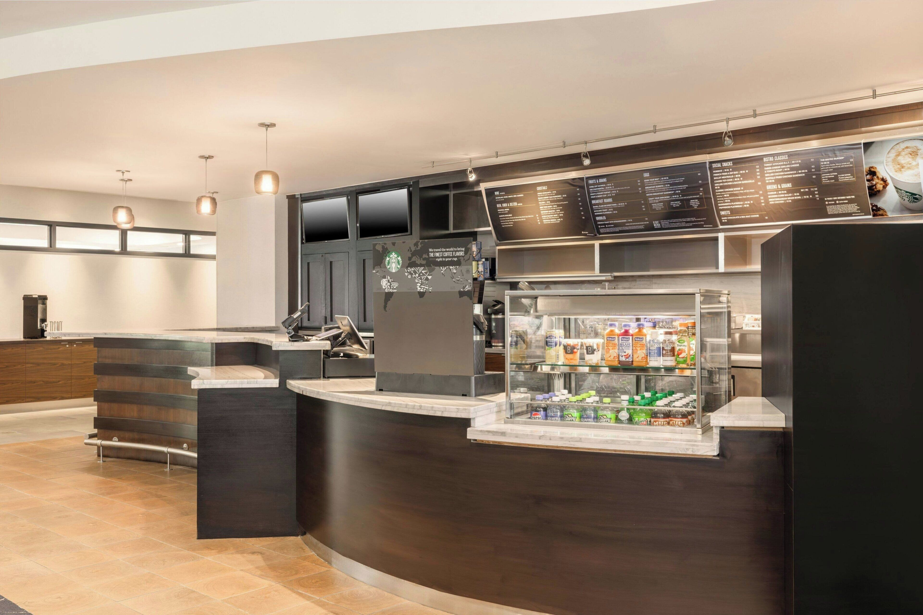 Interior moderno de café com balcão, quadro de cardápio e refrigerador com bebidas.